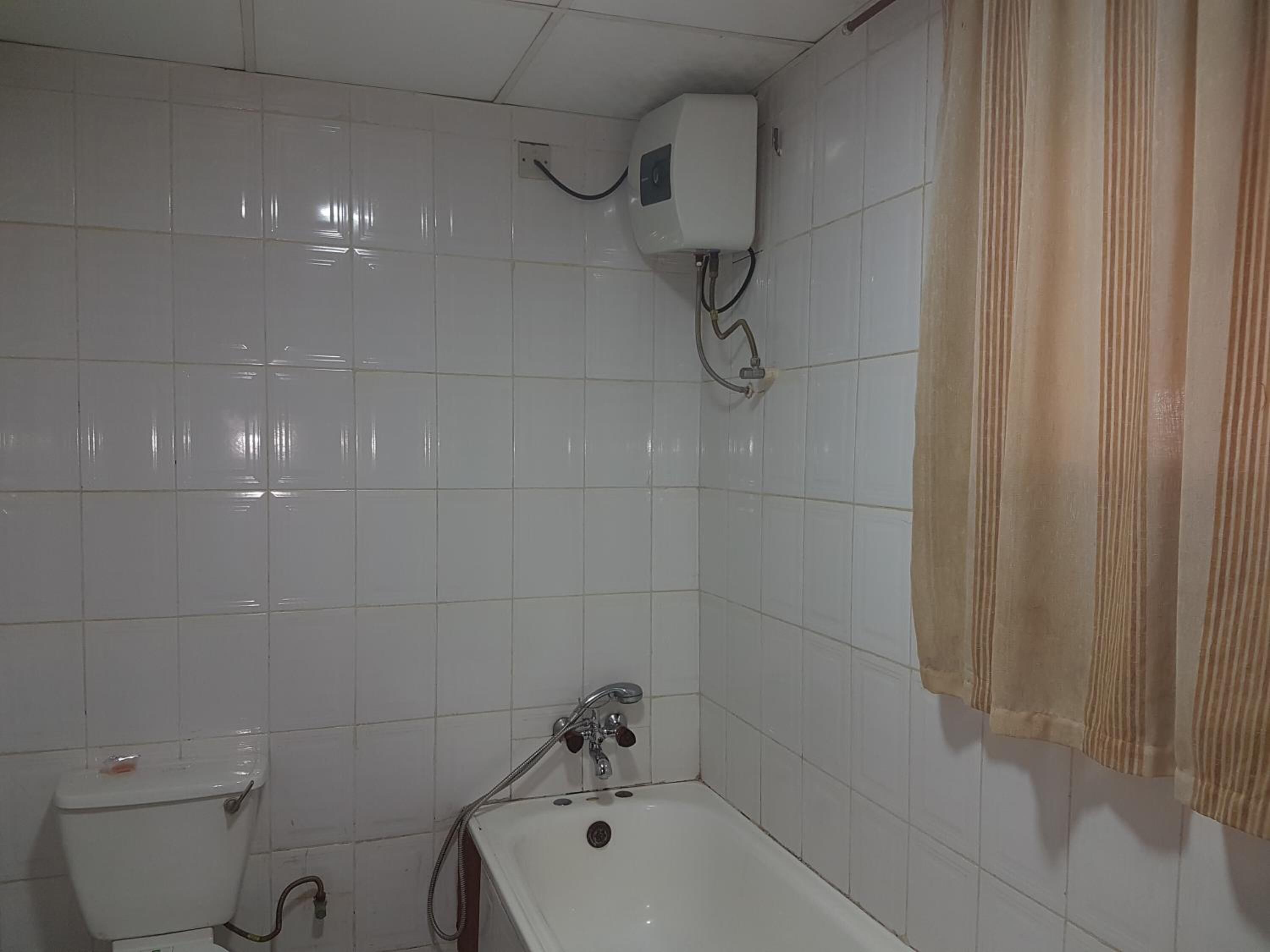 Casa de banho com azulejos brancos, sanita, lavatório e chuveiro.
