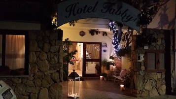 Um arco de pedra com a placa "Hotel Fabry" acima de uma porta que dá acesso a um interior acolhedor e iluminado.