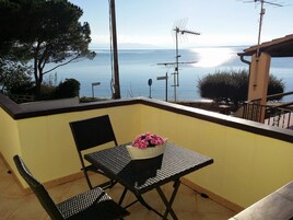 Uma varanda com mesa e cadeiras, um vaso de flores e vista para o mar.