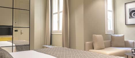 Quarto de hotel com uma cama grande, um sofá, uma mesinha e um espelho.