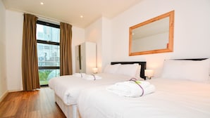 Quarto de hotel com duas camas, um espelho grande e vista para a paisagem urbana pela janela.