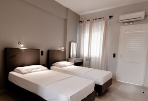 Quarto de hotel com duas camas de solteiro, uma mesa de cabeceira com espelho, ar condicionado e uma porta.