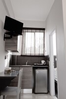 Uma cozinha compacta com micro-ondas integrado, um refrigerador pequeno e uma janela com cortinas leves.