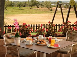 Mesa de café da manhã montada ao ar livre, com vista para um campo cercado e árvores.