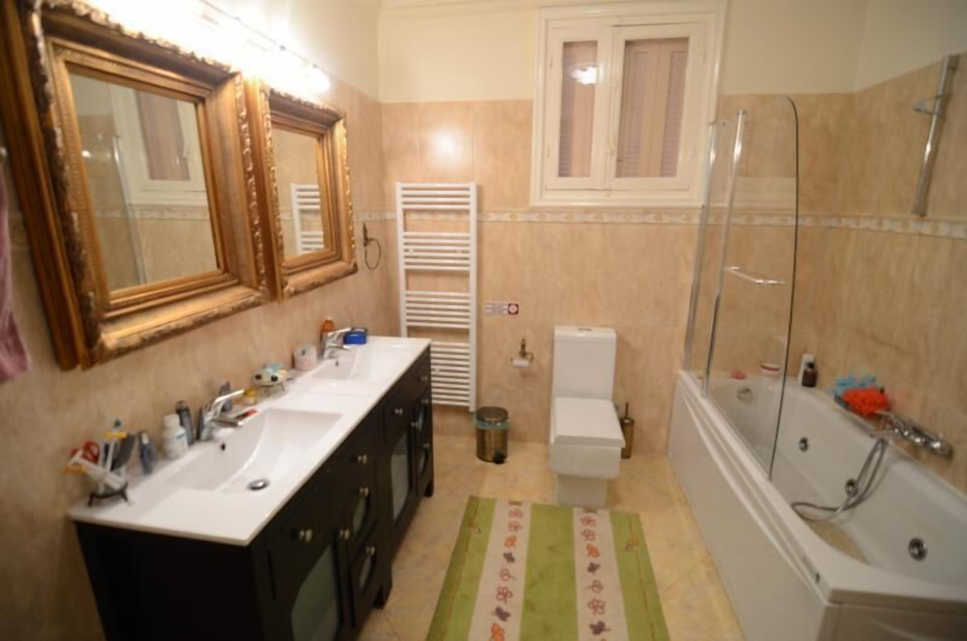 Casa de banho com duas pias, sanita, banheira e janela.