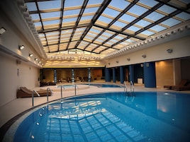 Piscina interior com teto de vidro, espreguiçadeiras e interior banhado pelo sol.