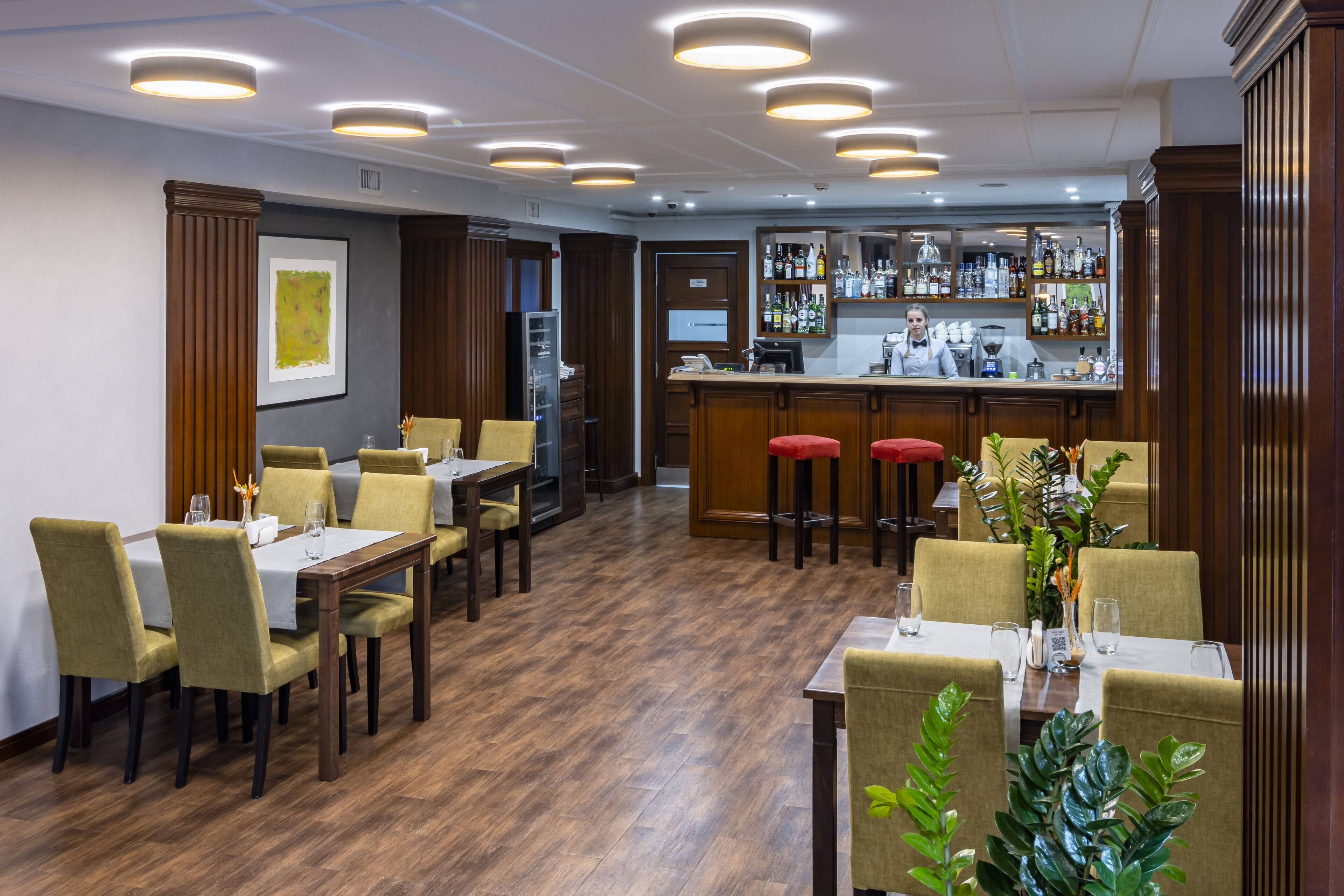 Um restaurante com piso de madeira, cadeiras amarelas e um bar com um barman.