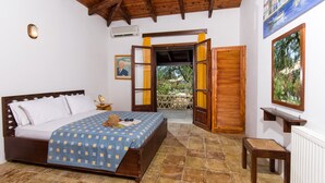 Quarto com cama de madeira, uma mesinha de cabeceira, janela com vista para vegetação e porta que dá para o exterior.