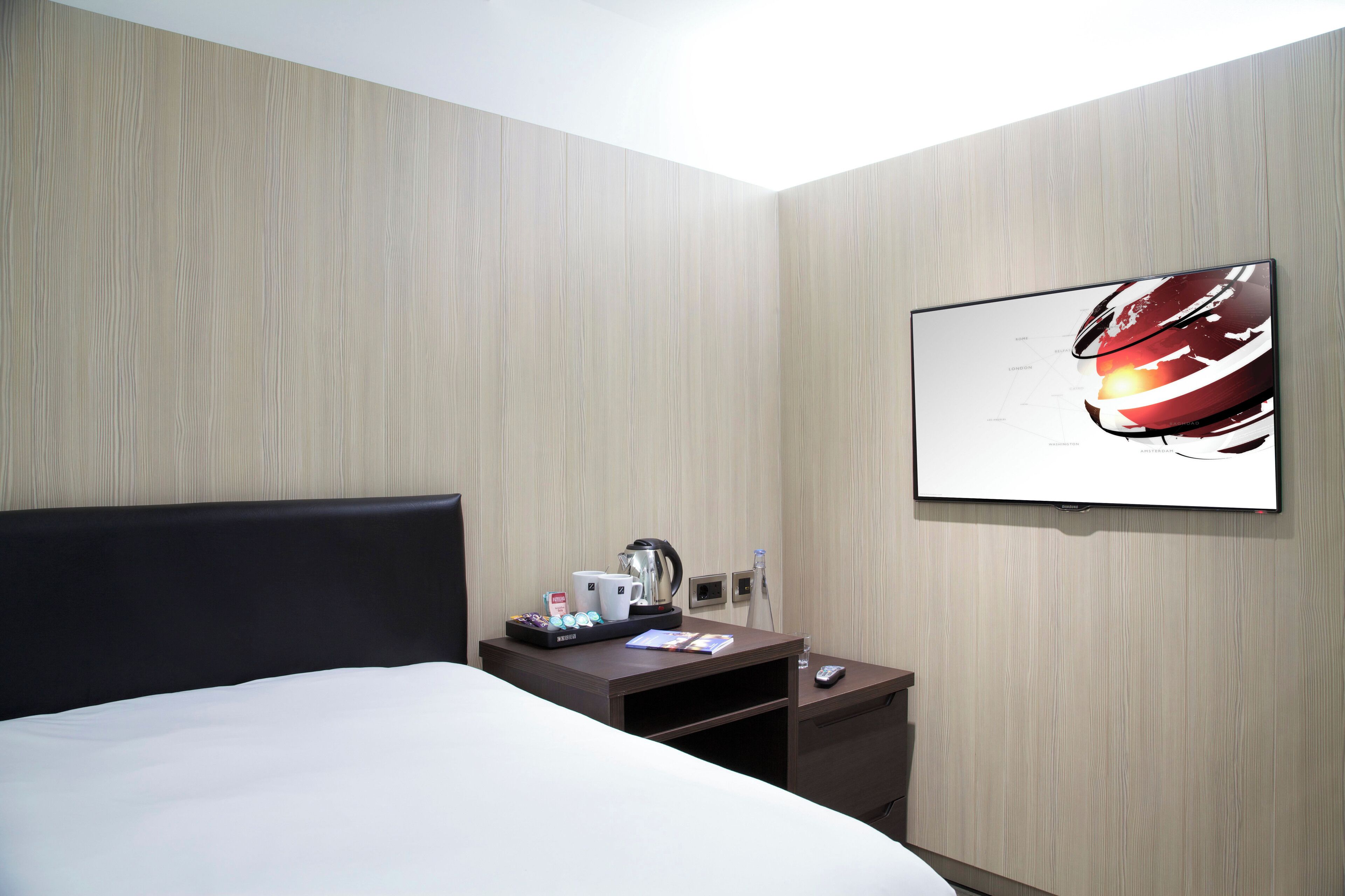 Quarto de hotel com cama, mesa com cafeteira, chávenas e comando à distância.