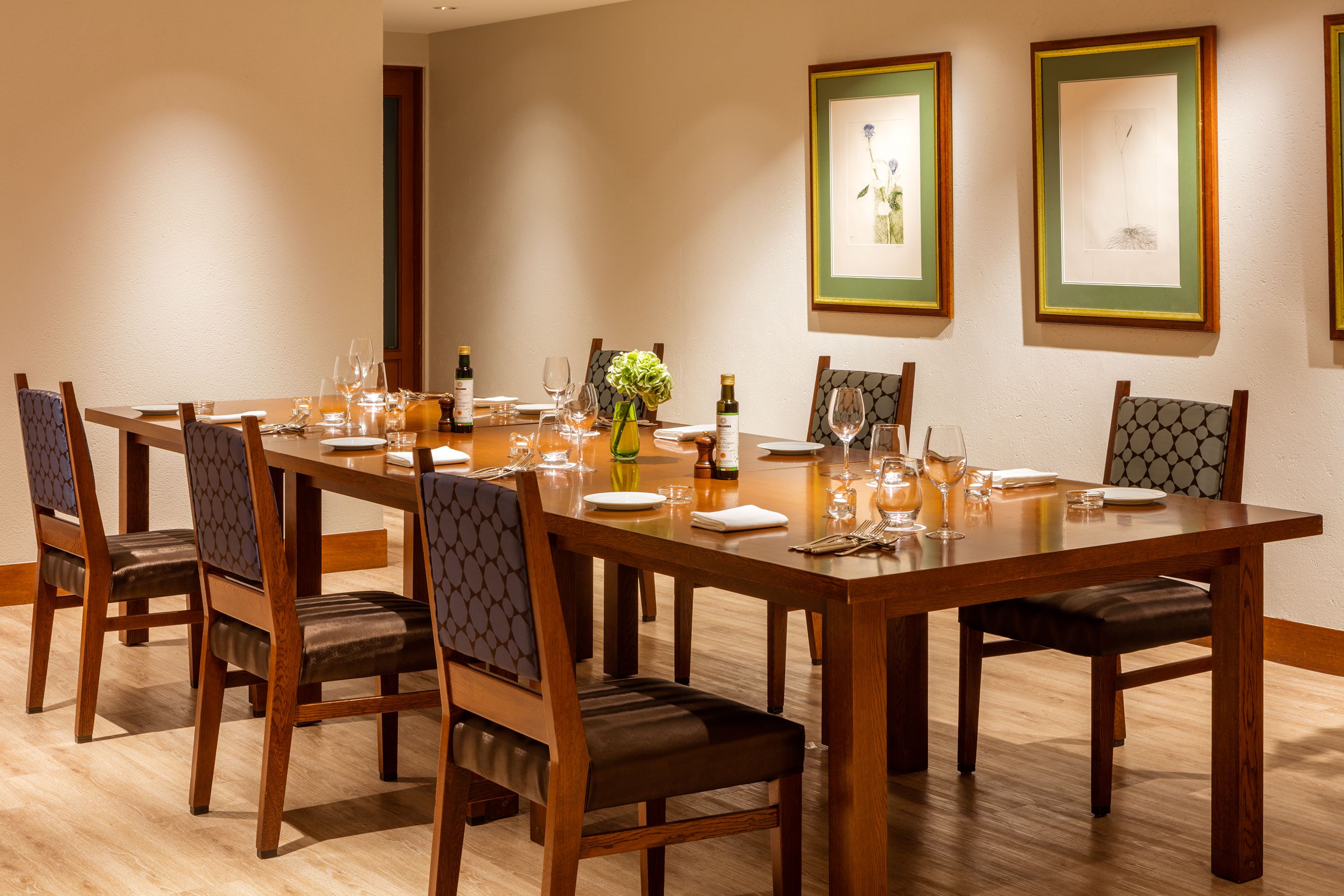 Uma sala de jantar com uma mesa de madeira comprida posta para uma refeição, rodeada por cadeiras estofadas.