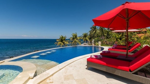 Uma piscina particular com borda curva, cadeiras de lounge vermelhas e um guarda-sol vermelho.