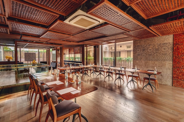 Uma sala de conferências ampla, com mesas e cadeiras de madeira, janelas grandes e um teto alto com design exclusivo.