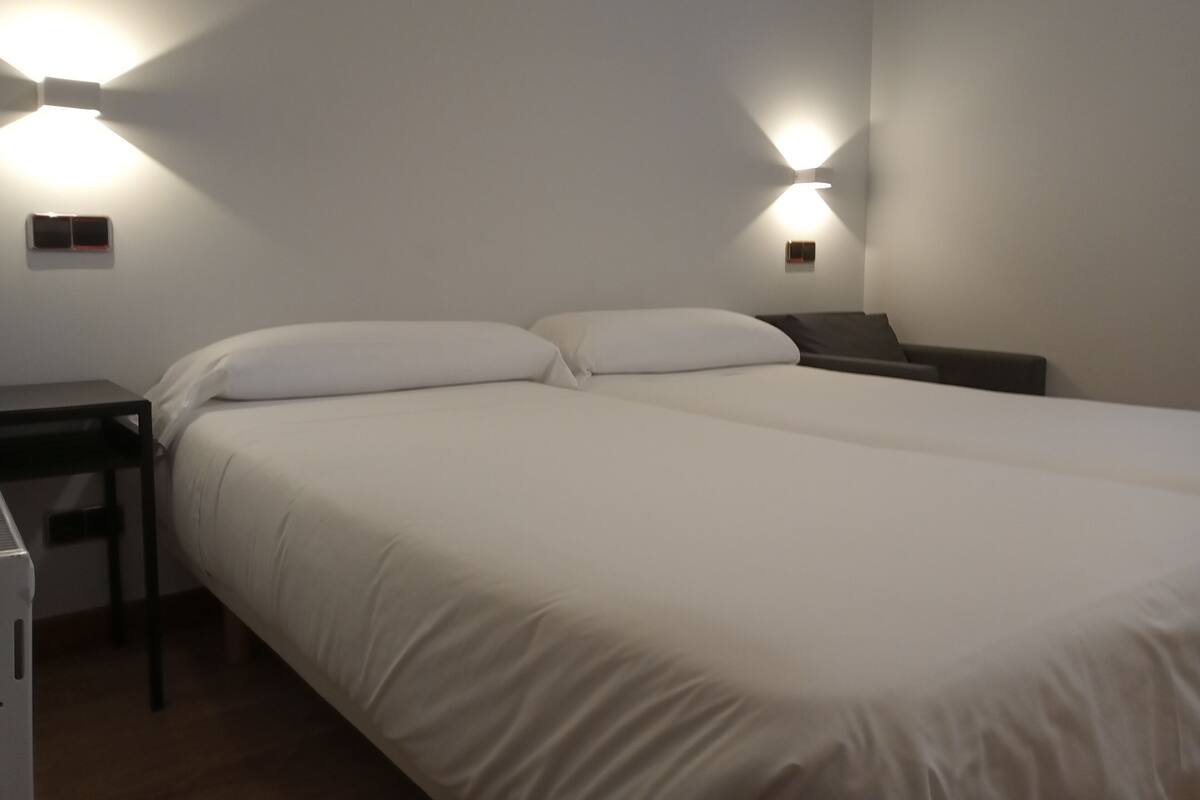 Quarto de hotel com cama, mesas de cabeceira e luminárias fixadas na parede.