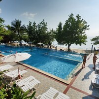 Piscina com espreguiçadeiras e guarda-sóis, cercada por árvores e vista para a praia.