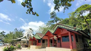 Um imóvel à beira-mar com vários edifícios de telhado vermelho, uma praia arenosa e vegetação exuberante.
