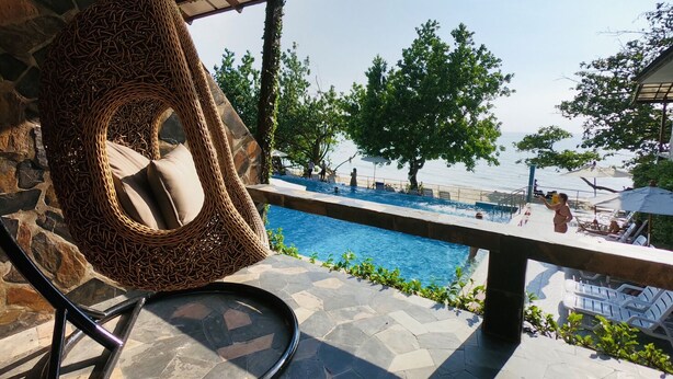 Uma cadeira suspensa perto de uma piscina, com paredes de pedra e vista para o mar.