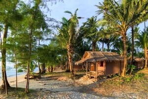 Um resort à beira-mar com cabanas de telhado de palha, palmeiras e uma praia de areia.
