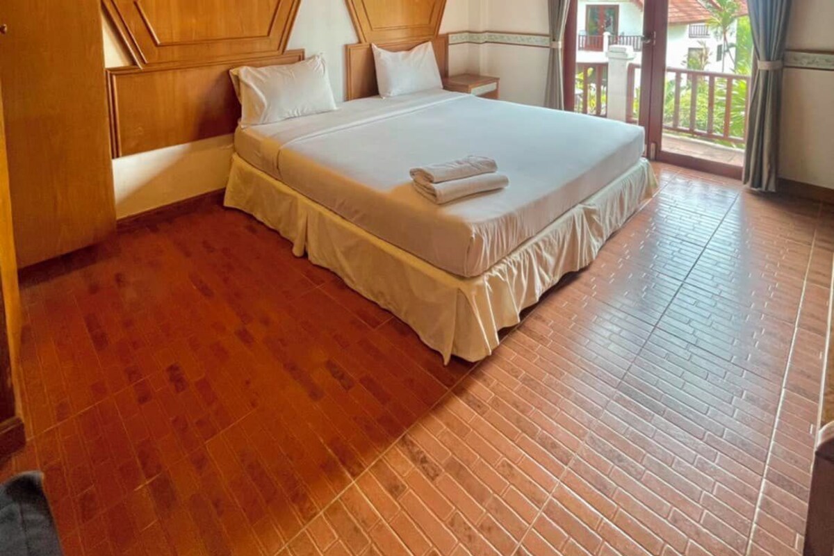 Quarto de hotel com cama grande, cabeceira de madeira e varanda com vista para uma casa.