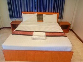 Cama bem arrumada com cabeceira de madeira, duas mesas de cabeceira e um fundo de cortina azul.