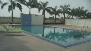 Piscina com água azul cristalina, rodeada por palmeiras e um deck revestido com azulejos.