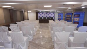 Uma sala de conferências com fileiras de cadeiras brancas e um palco na frente.