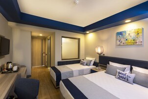 Quarto de hotel com duas camas, uma escrivaninha com chaleira, luminária e mapa na parede.