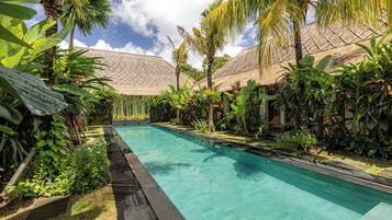 Piscina cercada por plantas tropicais e estruturas com telhados de palha.