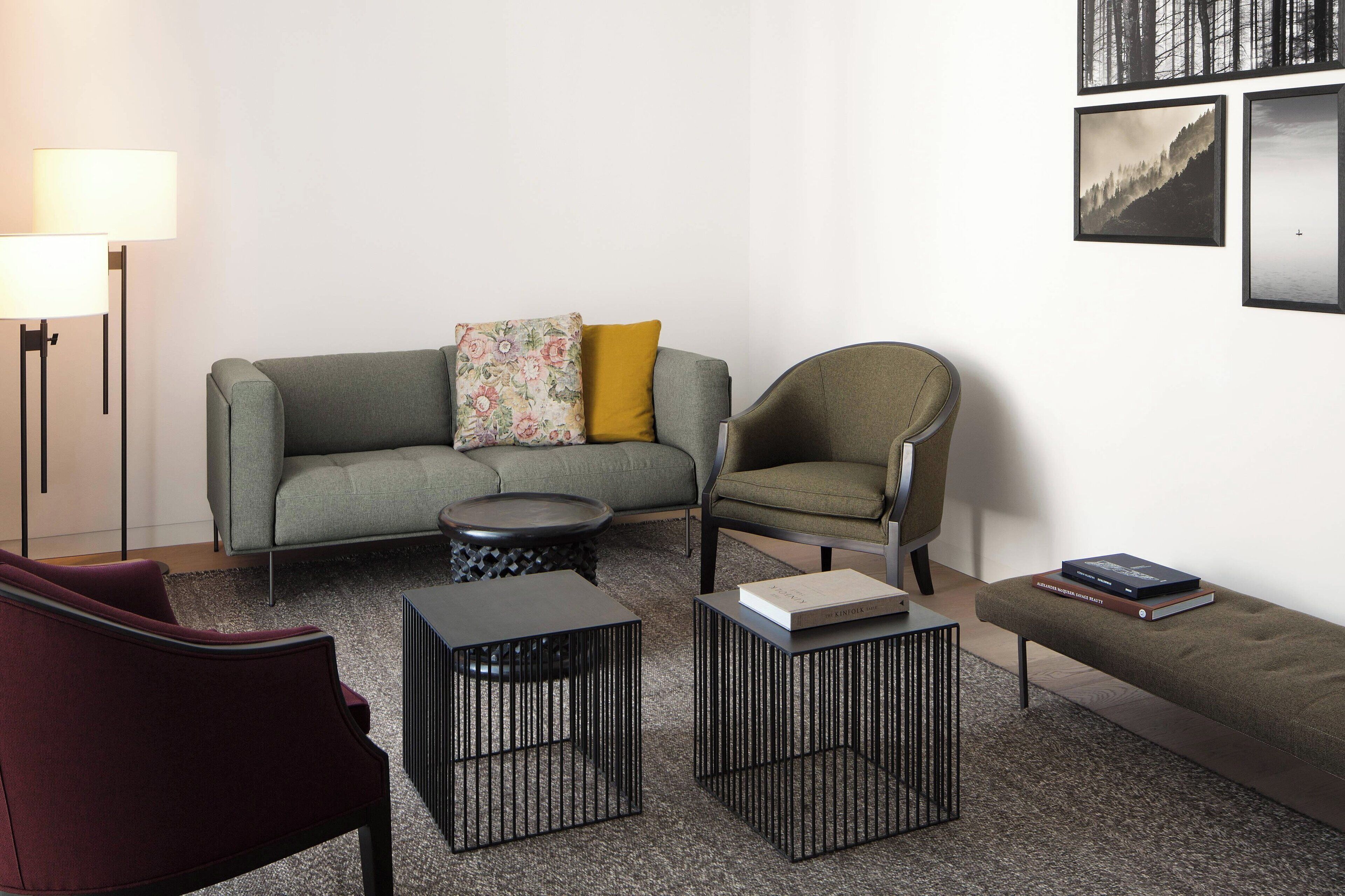 Uma sala de estar moderna com um sofá cinzento, uma poltrona vermelha, uma mesa de centro preta e uma mesa lateral. Há duas luminárias de chão e uma estante com livros.