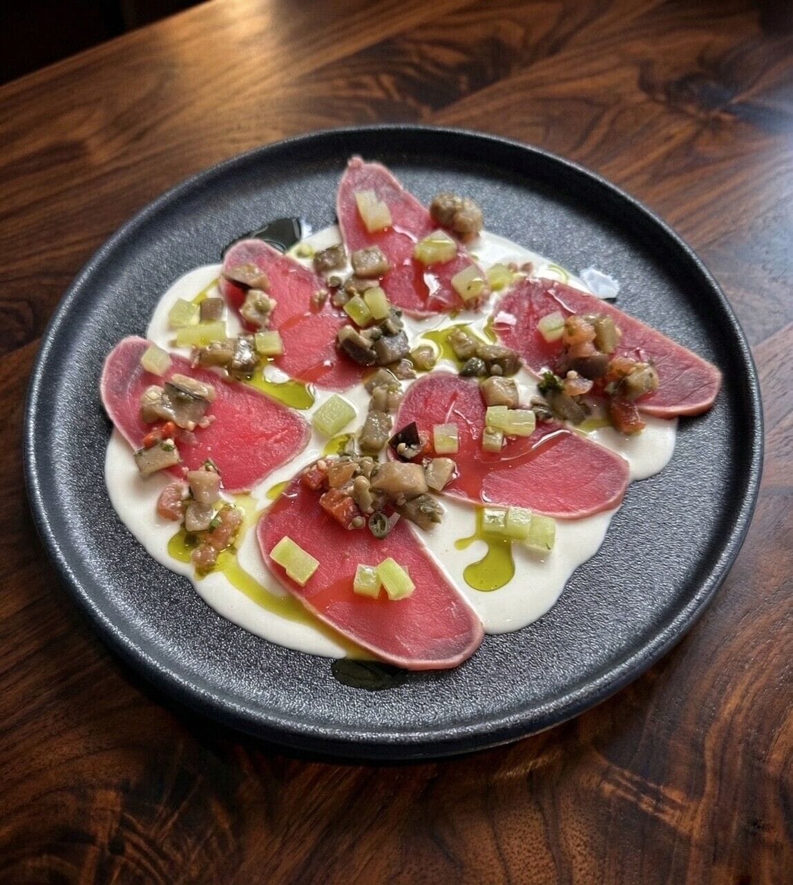 Prato de comida com fatias de carne e legumes sobre um prato escuro.