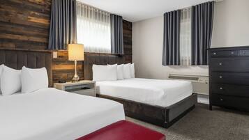 Quarto de hotel com duas camas, um banco vermelho, uma cômoda e um abajur.