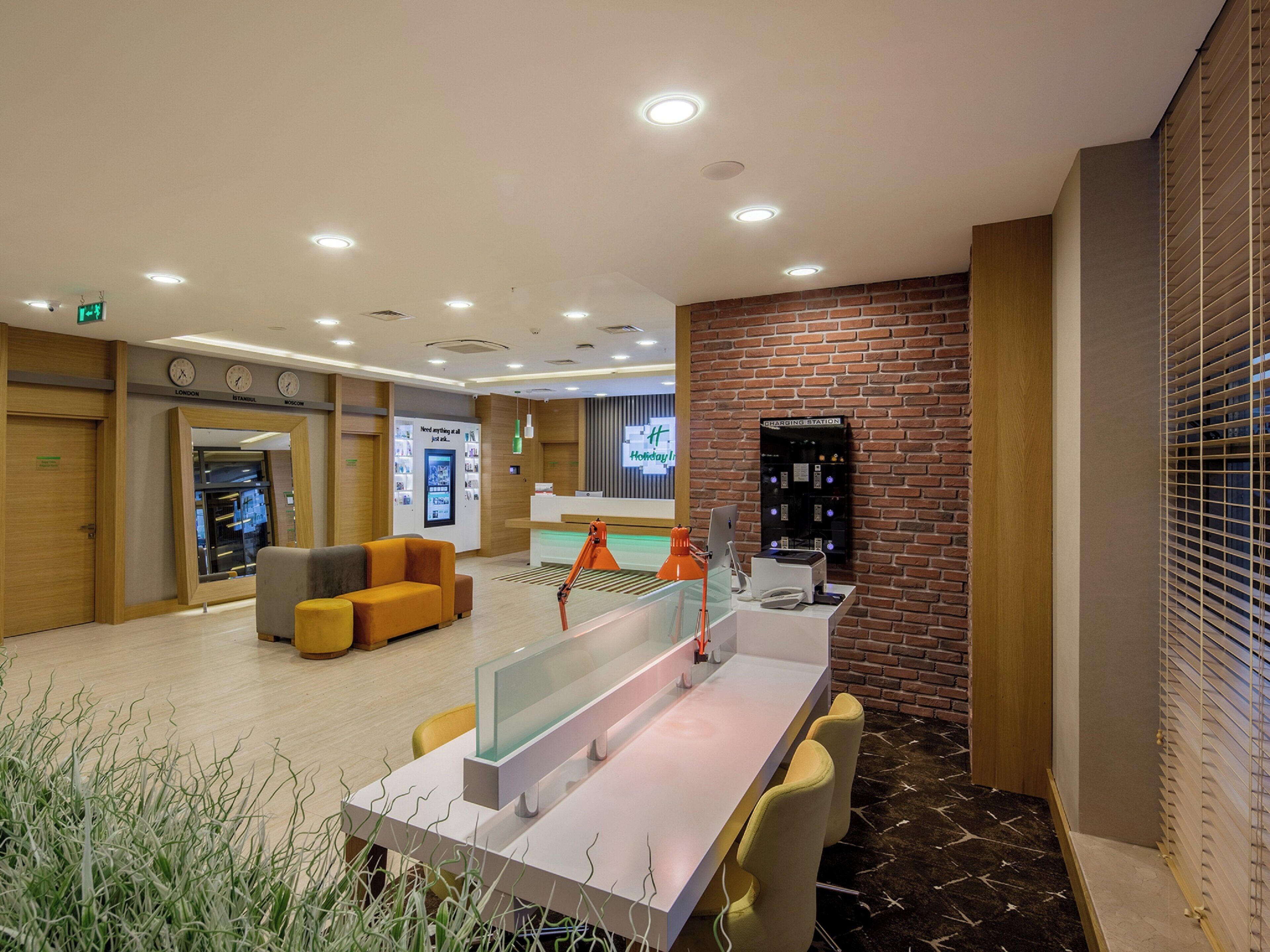 Uma área de recepção de hotel com design moderno, incluindo balcão de atendimento, área de estar e parede de destaque em tijolo.