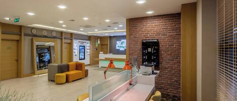 Uma área de recepção de hotel com design moderno, incluindo balcão de atendimento, área de estar e parede de destaque em tijolo.