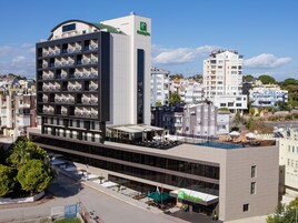 Um hotel moderno com várias varandas, uma piscina no terraço e uma área de estar ao ar livre coberta.