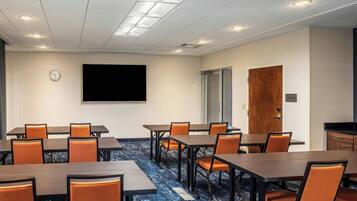 Uma sala de conferência com mesas, cadeiras, um relógio, uma tela e um armário.