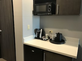 Uma cozinha compacta com micro-ondas, cafeteira e miniatura de geladeira.