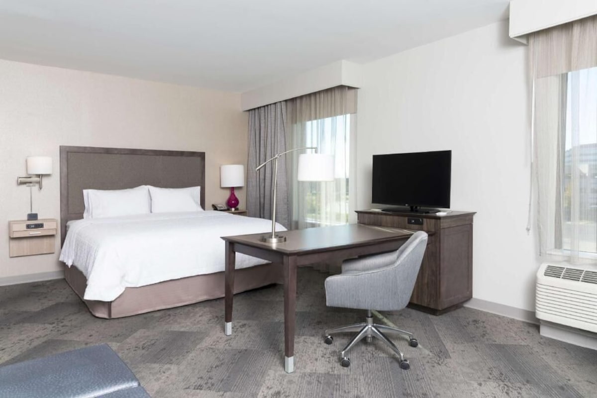 Quarto de hotel com cama, escrivaninha, cadeira, televisão e ar condicionado.