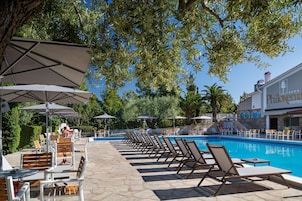 Área de piscina com espreguiçadeiras e guarda-sóis, piscina e um edifício com a placa "Philoxenia Hotel".