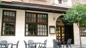 Um edifício com área de café e mesas e cadeiras de plástico ao ar livre.