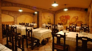 Um restaurante com várias mesas e cadeiras, arcos de tijolo e um mural na parede.