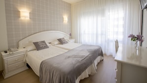Quarto de hotel com uma cama grande, mesas de cabeceira, um espelho e uma janela com cortinas leves.