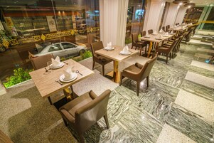 Um restaurante com várias mesas e cadeiras, vista para a rua e piso de azulejos.