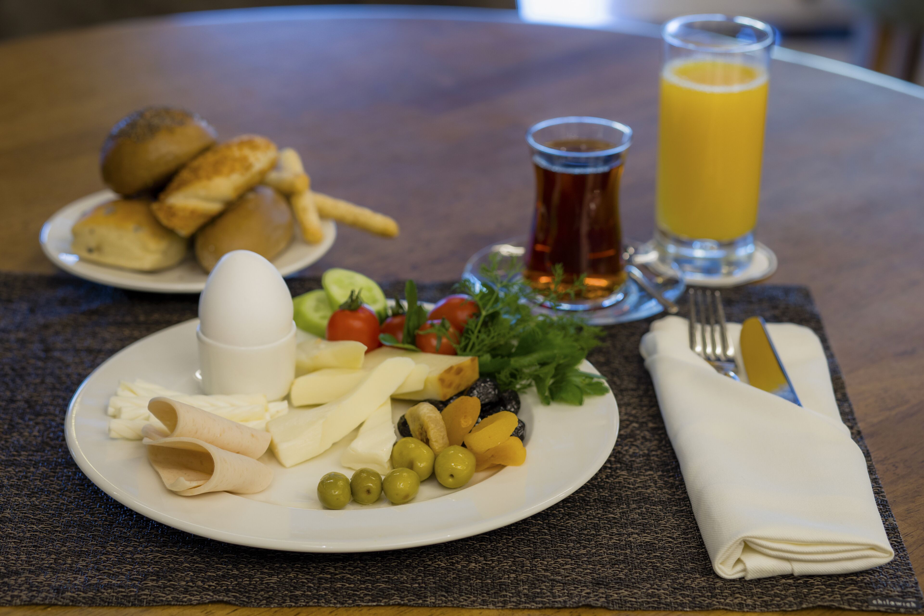 Prato de pequeno-almoço com ovos, queijo, azeitonas, tomates e vegetais, acompanhado por um copo de sumo de laranja e uma chávena de chá.