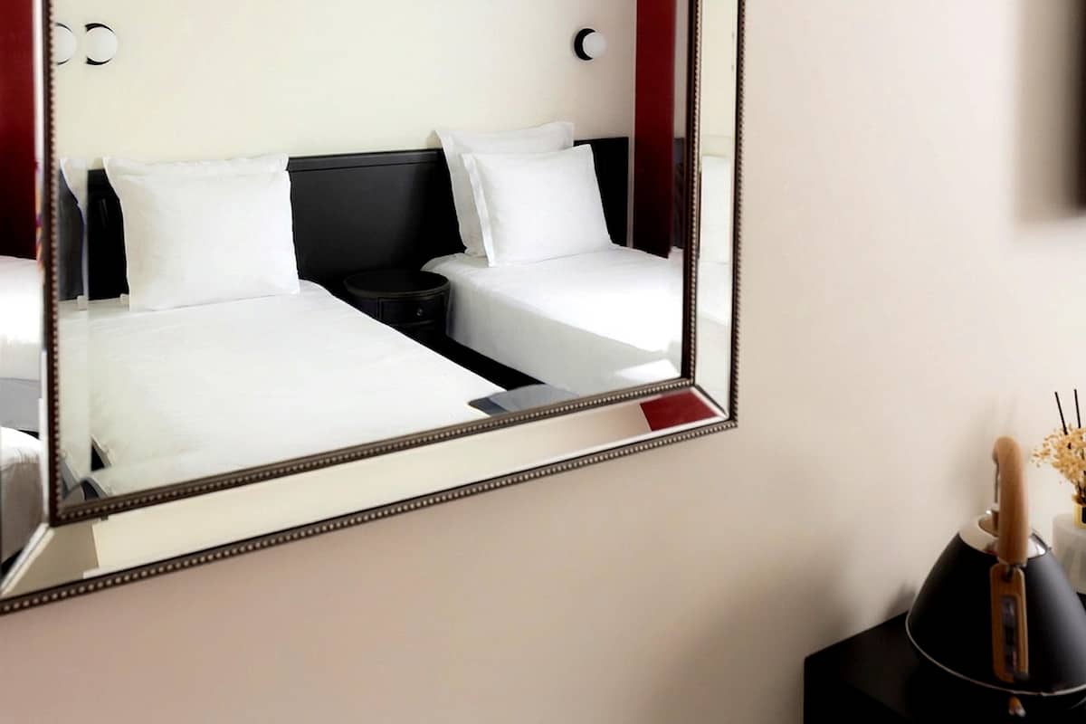 Quarto de hotel com uma cama, mesa de cabeceira e espelho refletindo o aposento.