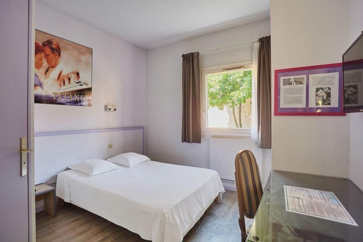 Um quarto com cama, escrivaninha, cadeira, janela com cortinas e um pôster na parede.