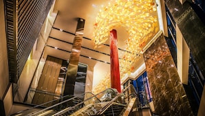 Interior moderno com um elevador em vidro, um pilar vermelho e uma instalação luminosa decorativa.