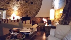 Um quarto acolhedor com parede de pedra, lareira, sofá e mesa de centro com livros e objetos decorativos.