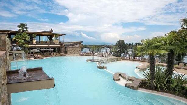 Piscina de resort com diversas atrações aquáticas, áreas de descanso e palmeiras.