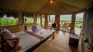 Um quarto coberto por uma tenda, com uma cama, uma cadeira de balanço e vista para o exterior.