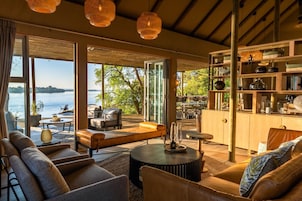 Uma sala de estar espaçosa com vista para um lago, mobiliada com sofás, uma mesa de centro e uma estante.
