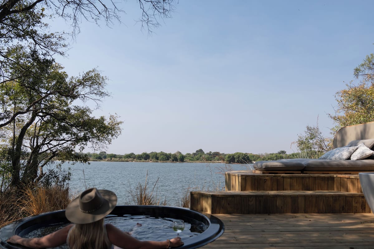 Um deck de madeira com uma banheira de hidromassagem, um sofá e vista para um lago.